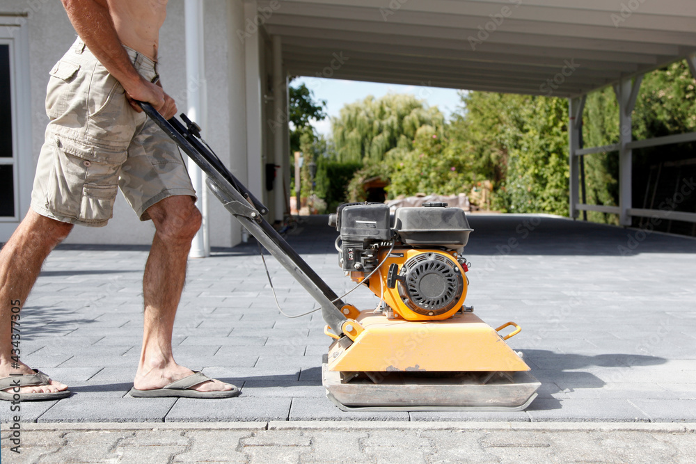 Male Worker using vibratory plate compactor to firm soil at worksite ...