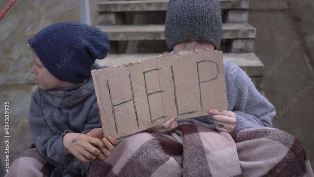 homeless boys sit with a help sign on the stairs in an abandoned place ...