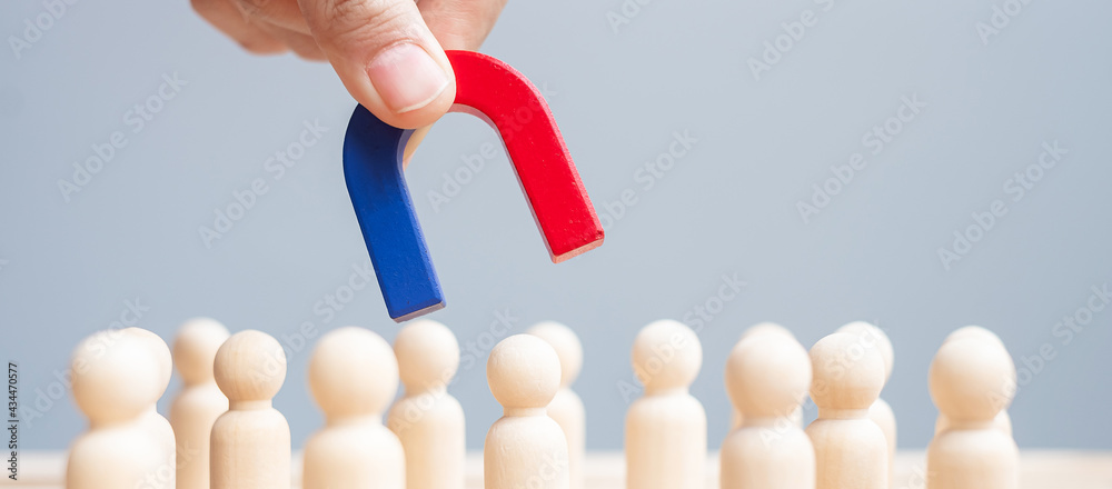 Business man hand holding magnet and pulling man wooden figure from the ...