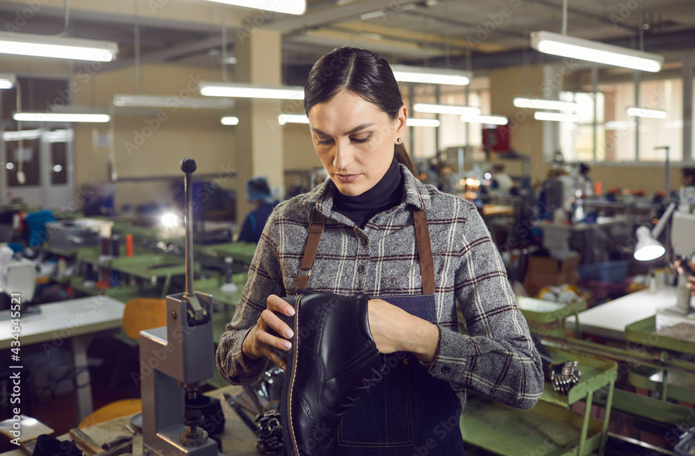 Serious female shoe factory worker checking quality of footwear. Woman ...