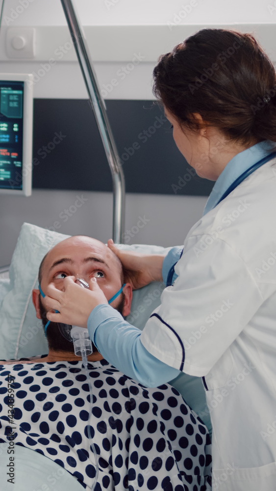 Sick man resting in bed while woman medic putting oxygen mask checking ...
