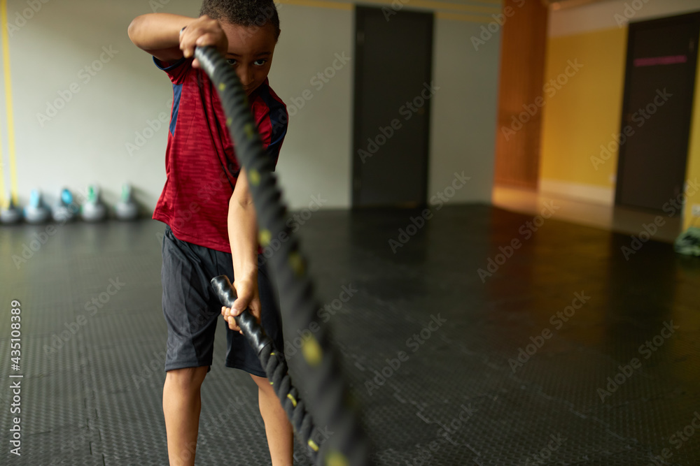 Strong fit Afro American boy exercising in gym using special tools for ...