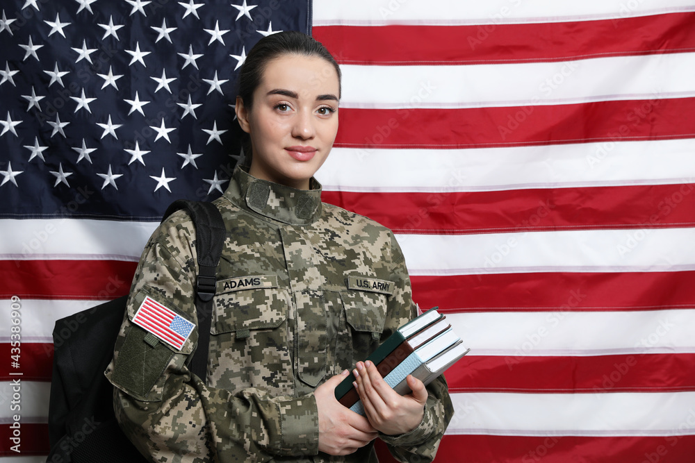 Female soldier with backpack and books near flag of United States ...