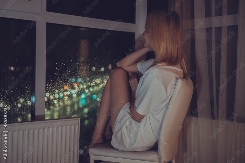 Young blonde woman in a white shirt sits on a chair with her chin ...