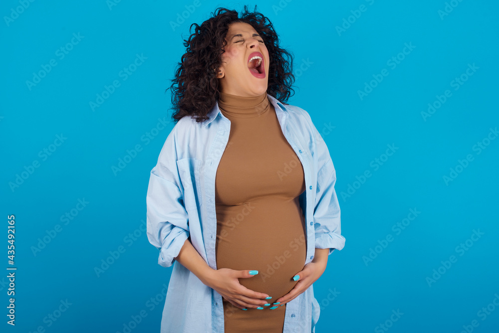 young Arab pregnant woman wearing dress against blue wall angry and mad ...