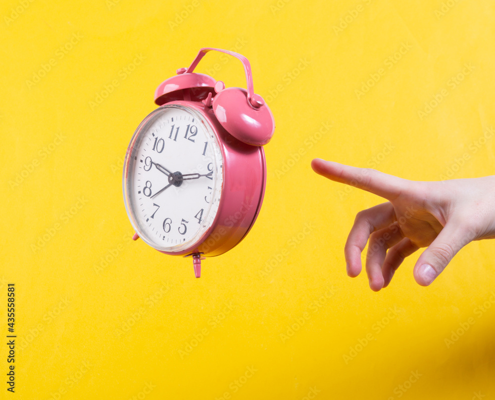 Hand and Levitating pink alarm clock on yellow background. Minimalistic ...