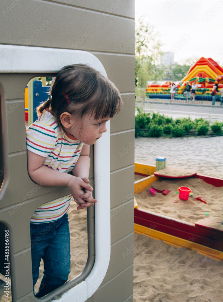 Serious child peeking out of a small house in the playground. The child ...