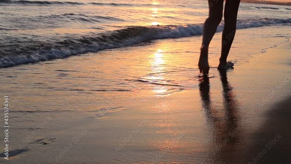 female feet walk on sea water with waves with foam along the sandy ...