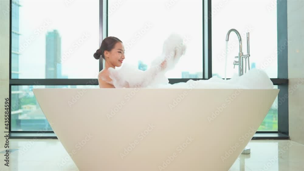 Asian woman foaming her body, she is lying in a bathtub full of foam on ...