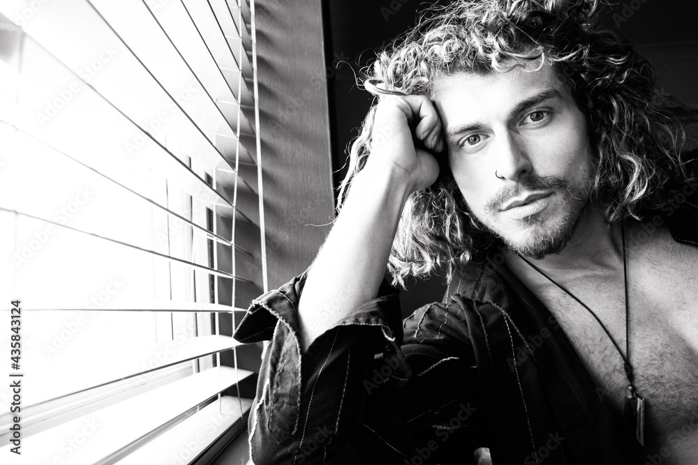 Handsome man with long hair and beard leaning on a windowsill next to a ...