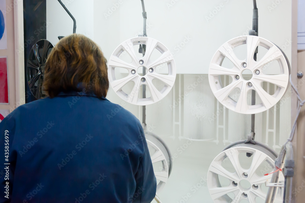 An employee of a wheel rim factory paints wheels with white paint in a ...