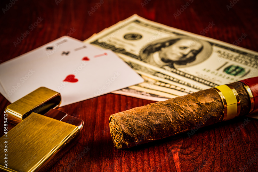 Cuban cigar and golden lighter with playing cards and pack of dollars ...