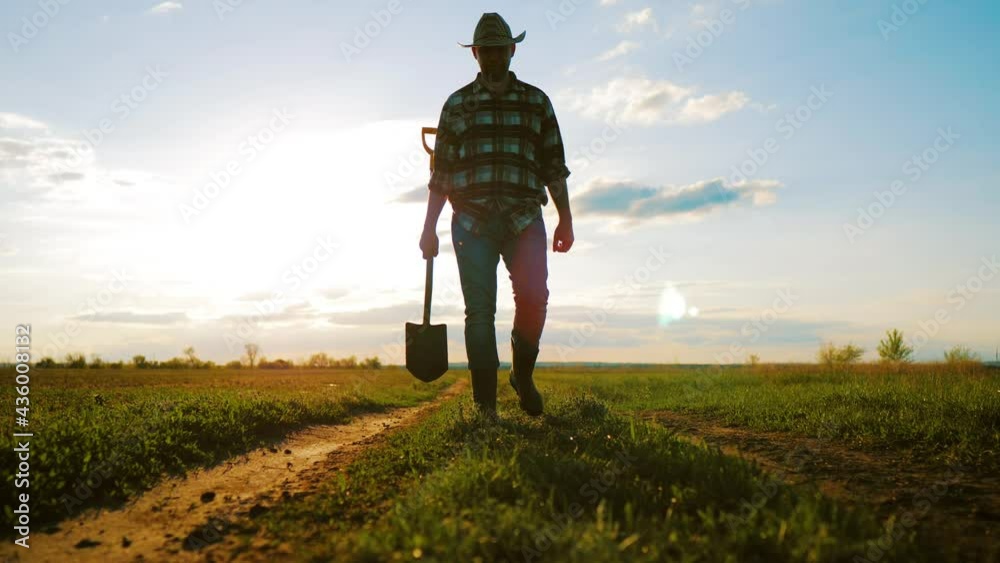Farm agriculture concept. Farmer with a shovel in rubber boots walks ...