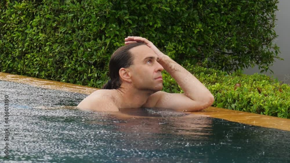 Introvert man stay in swimming pool under heavy rain, stare off into ...