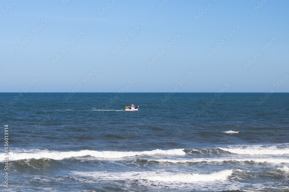 A small fishing boat sailing far away in the open Atlantic Ocean seen ...