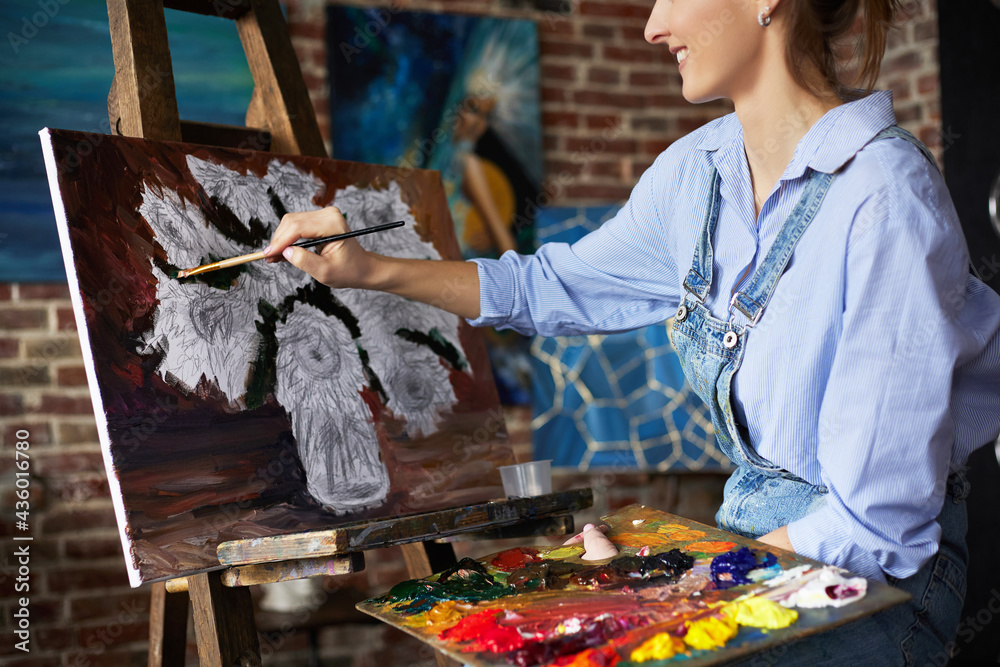 Young beautiful female artist painting still life with sunflower on ...
