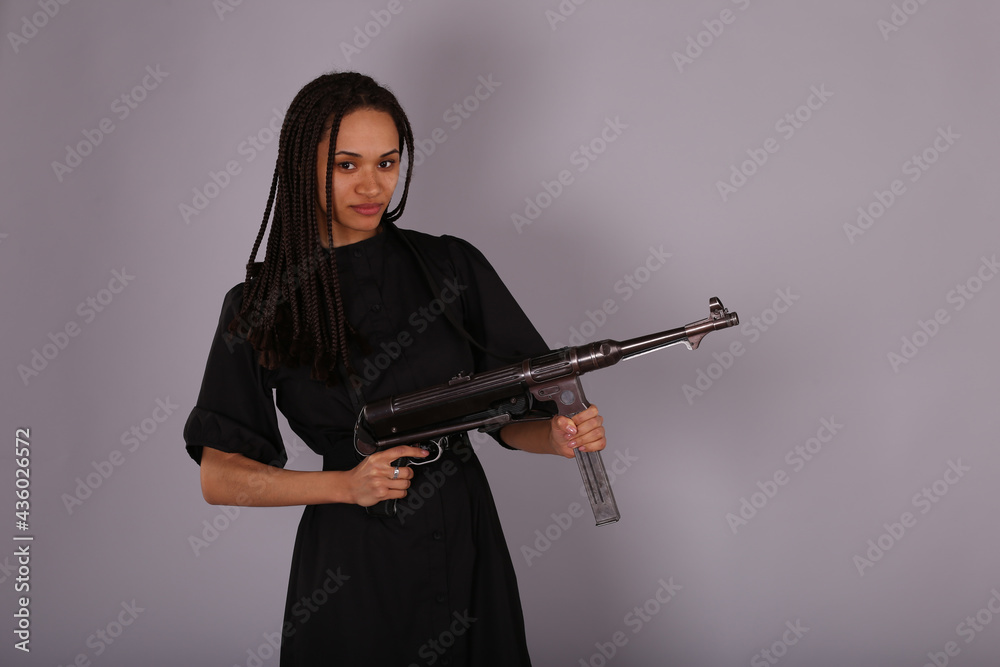 Curly woman in black dress with vintage submachine gun on grey ...
