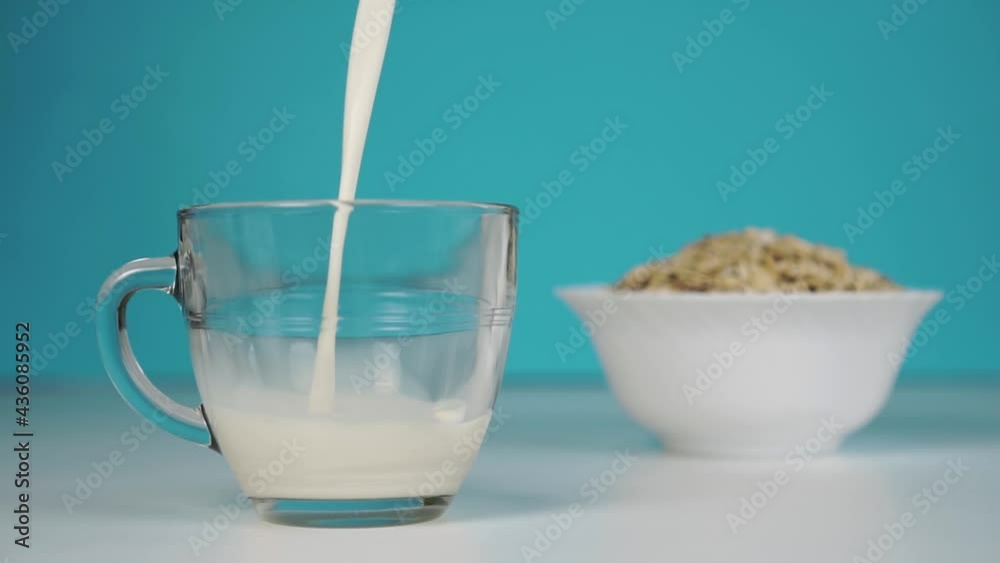 Pouring fresh milk into a glass on a blue background with splashes in ...
