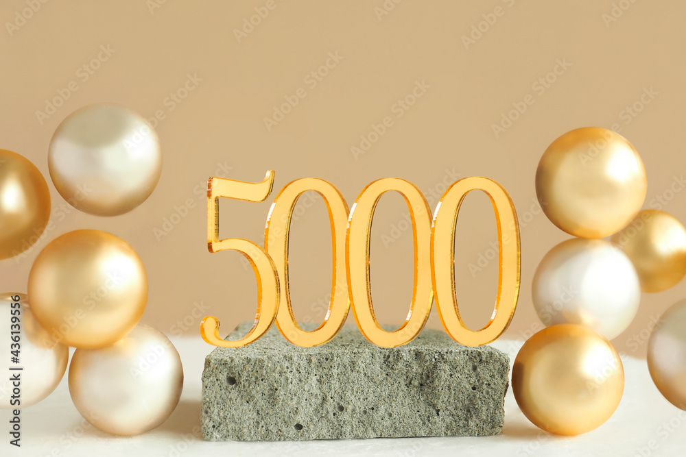 Number 5000 on a concrete podium and volumetric golden balls on a beige ...
