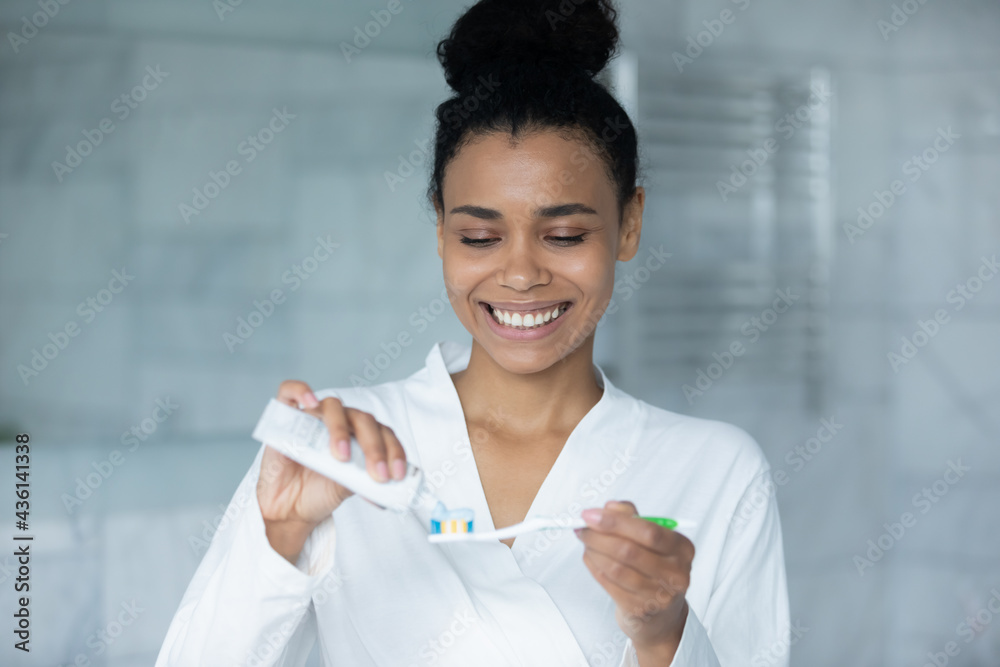 Happy young African American woman squeezing mint toothpaste from tube ...