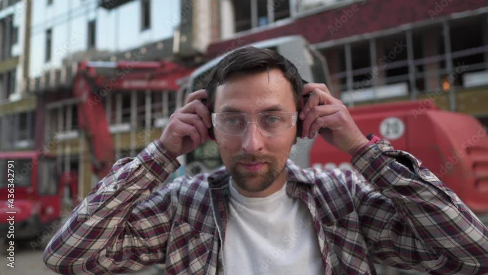 Builder in front of construction machinery puts hearing protection on ...