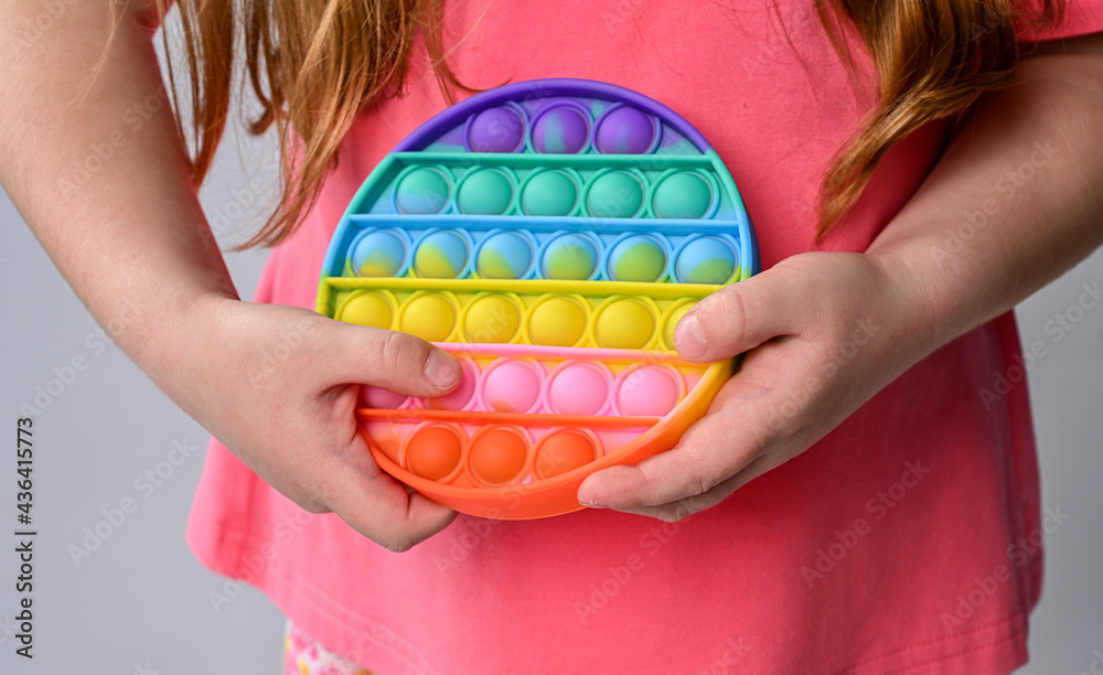Girl kid hand hold new sensory toy - pop it. Rainbow color, concave and ...