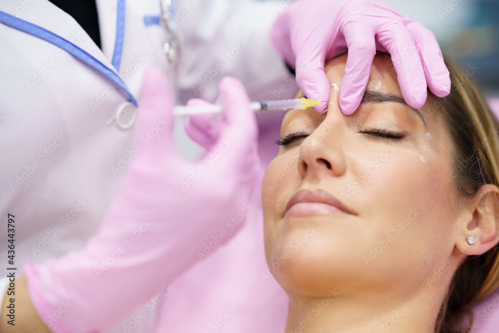 Aesthetic doctor injecting botulinum toxin into the forehead of her ...