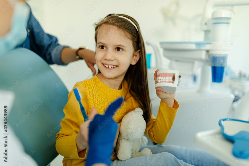 Cute little girl is holding a jaw model and a toothbrush and practicing ...