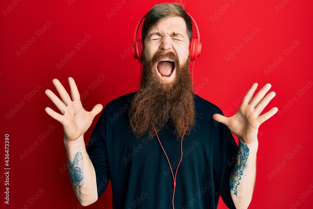 Redhead man with long beard listening to music using headphones ...