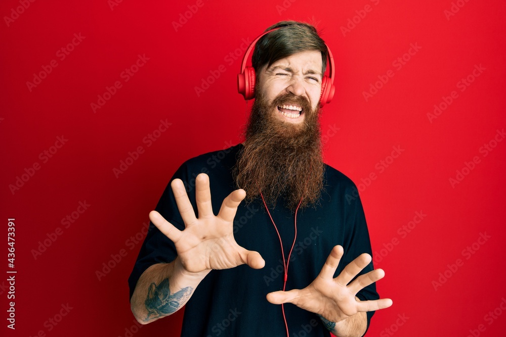 Redhead man with long beard listening to music using headphones ...