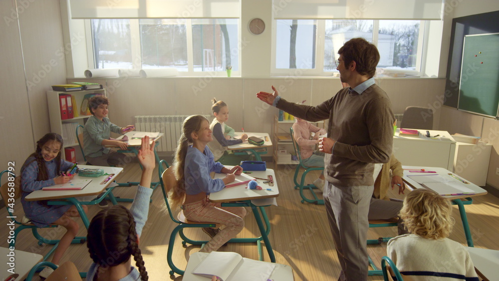 Teacher asking questions to students in class. Schoolchildren raising ...