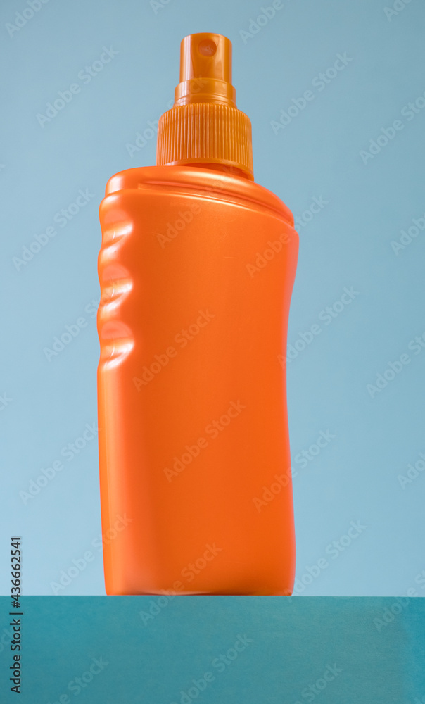 Orange bottle of sunscreen on the podium on a blue background. Summer ...