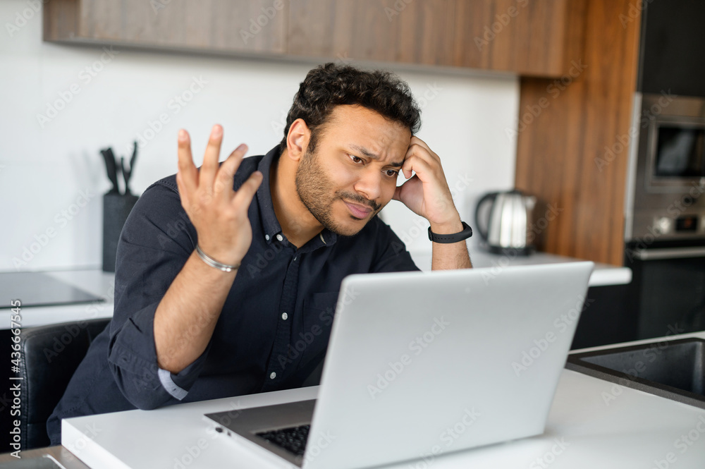 Confused indian man in smart casual shirt looking at the laptop screen ...