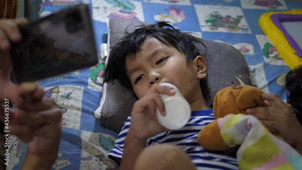 4K Asian child boy lying on bed with bottle milk, watching on ...