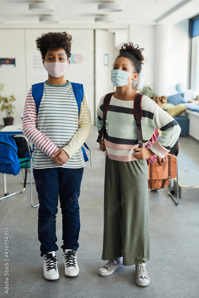 Full length portrait of two kids wearing masks in school classroom and ...