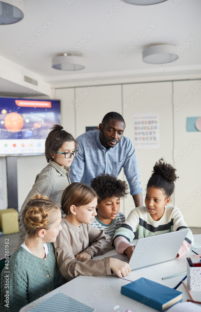 Vertical shot of diverse group of children using laptop together at ...