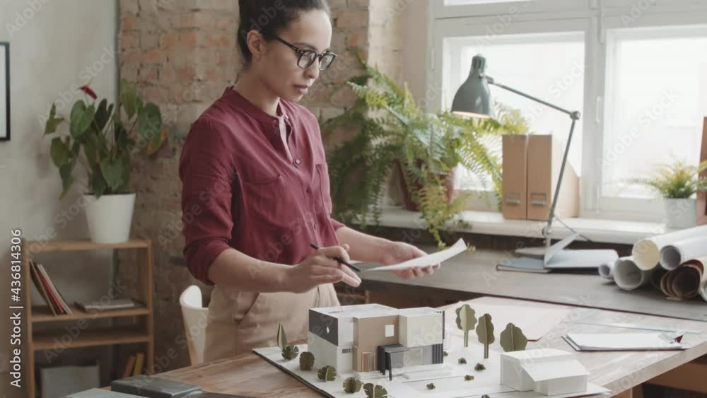 Tilt-up slowmo of female architect standing at her work desk in modern ...