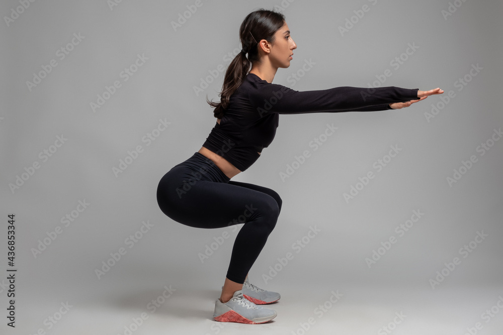 Side view of girl doing squats on grey background Stock Photo | Adobe Stock