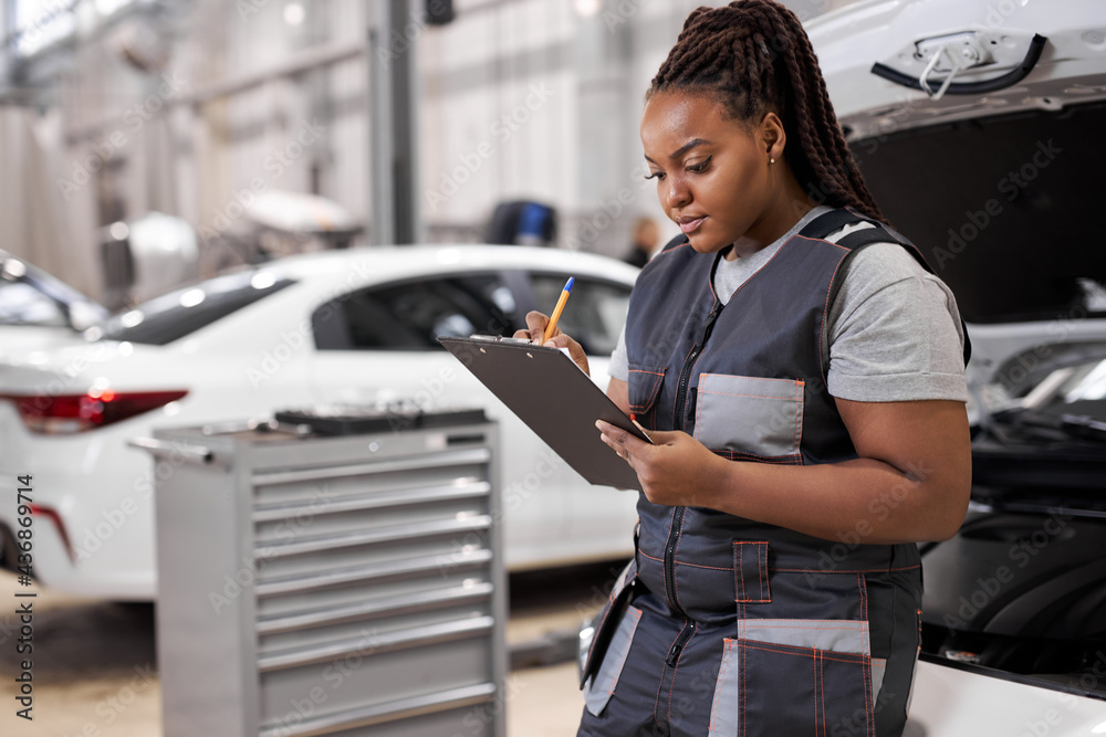 Afro Female mechanic engineer holding checklist paper and taking notes ...