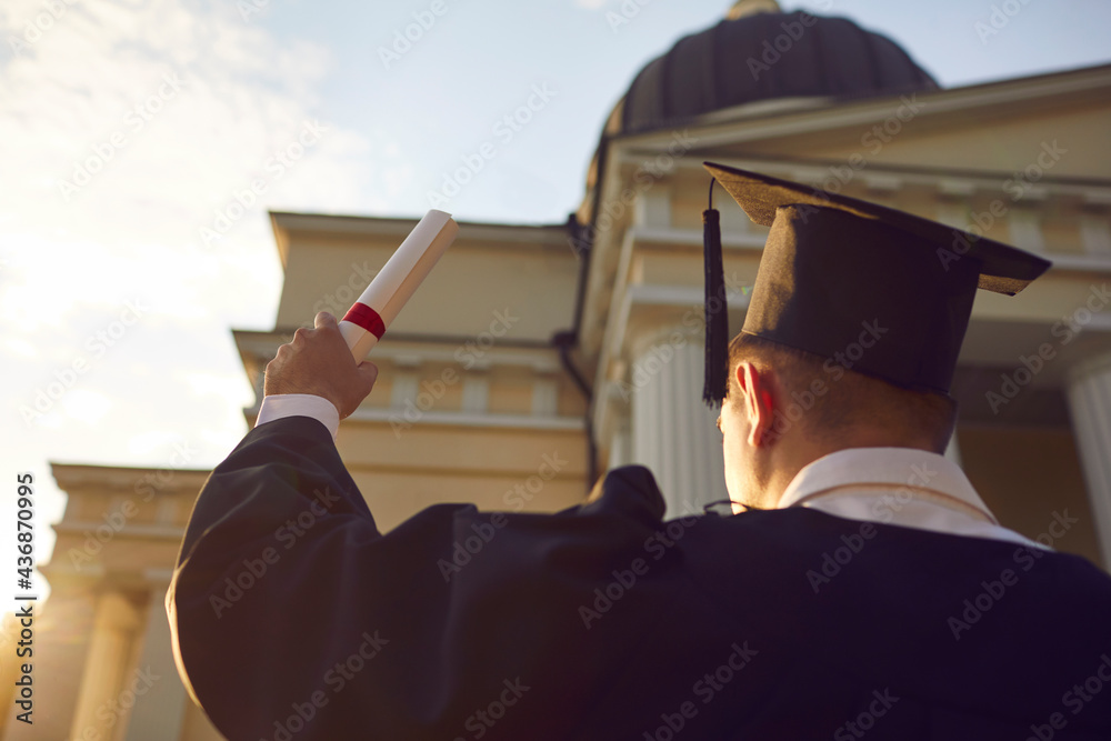 Student wearing gown and academic hat raising diploma degree ...