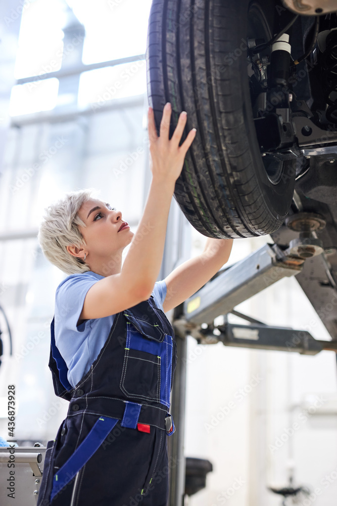 Caucasian female auto mechanic changing wheel tire in car in garage ...