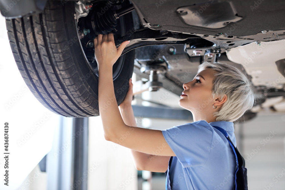 Caucasian female auto mechanic changing wheel tire in car in garage ...