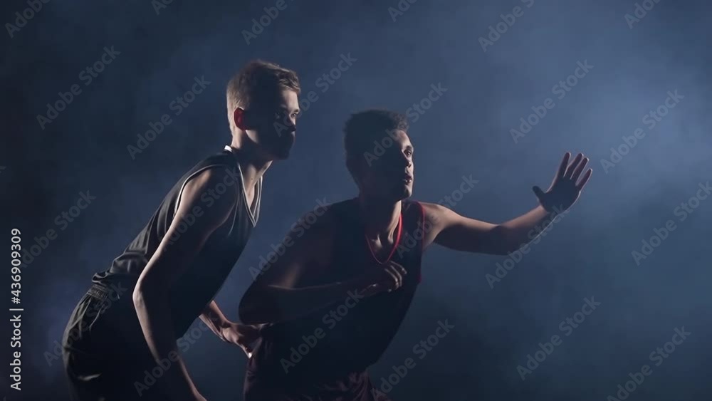 Two young athletes practice basketball in a dark smoky studio under the ...