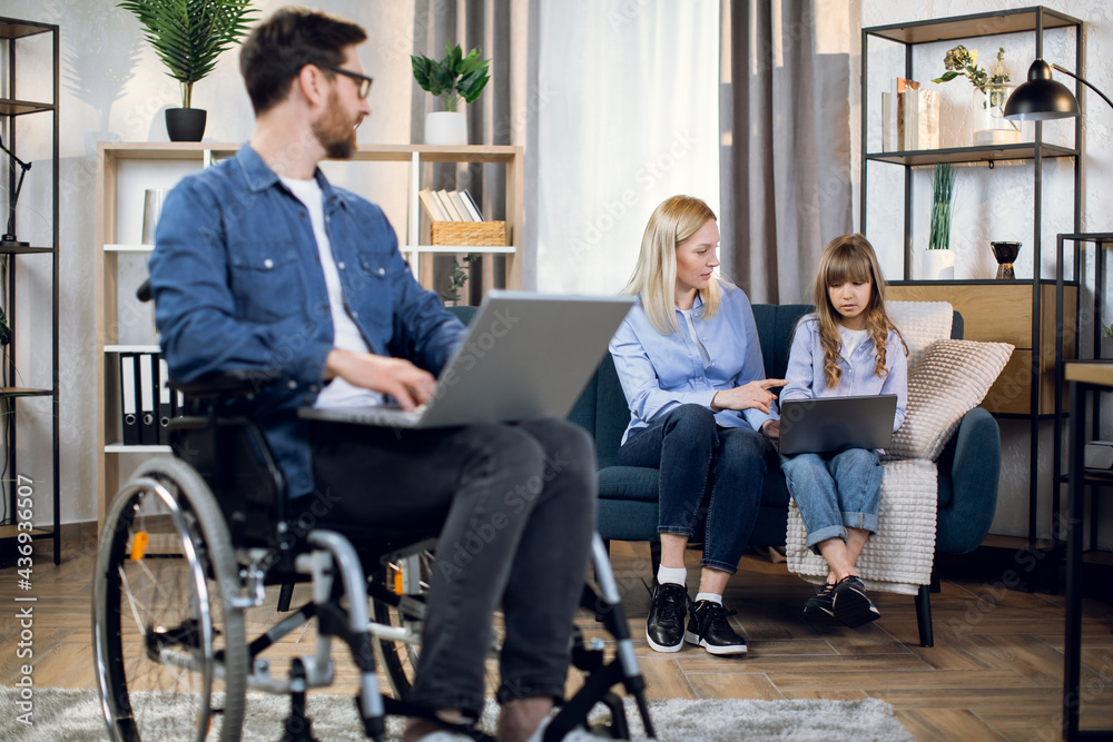 Disabled bearded man working on modern laptop while his wife and ...