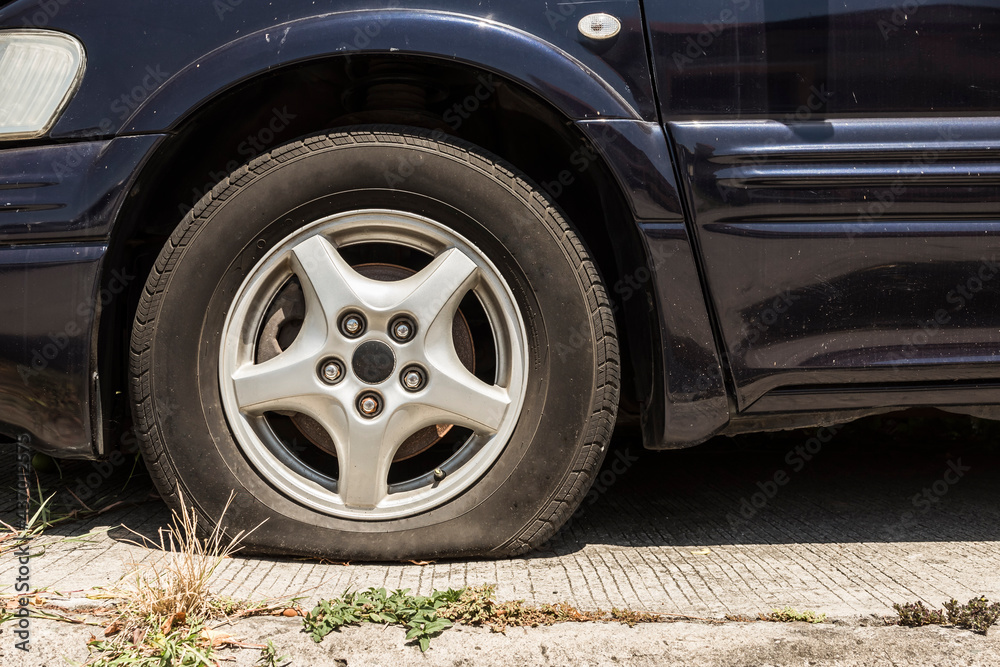 An old car with a flat or deflated tire. A sedan parked by a concrete ...