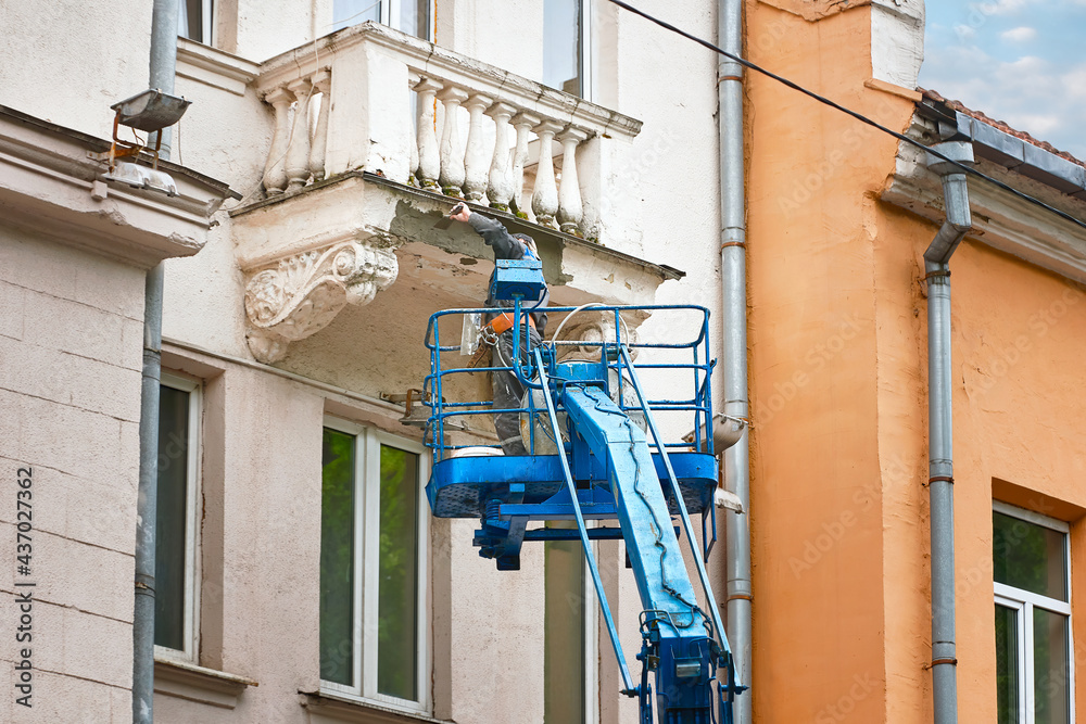 Worker repairing balcony, historic architecture of old facade. Plaster ...