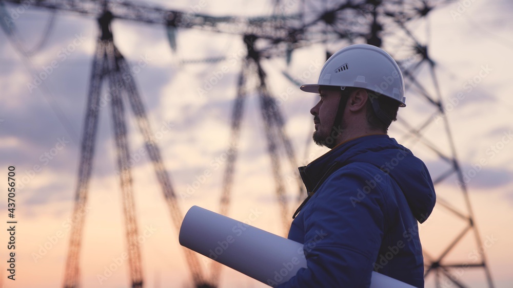 An electrician on the background of high towers of power plants looks ...
