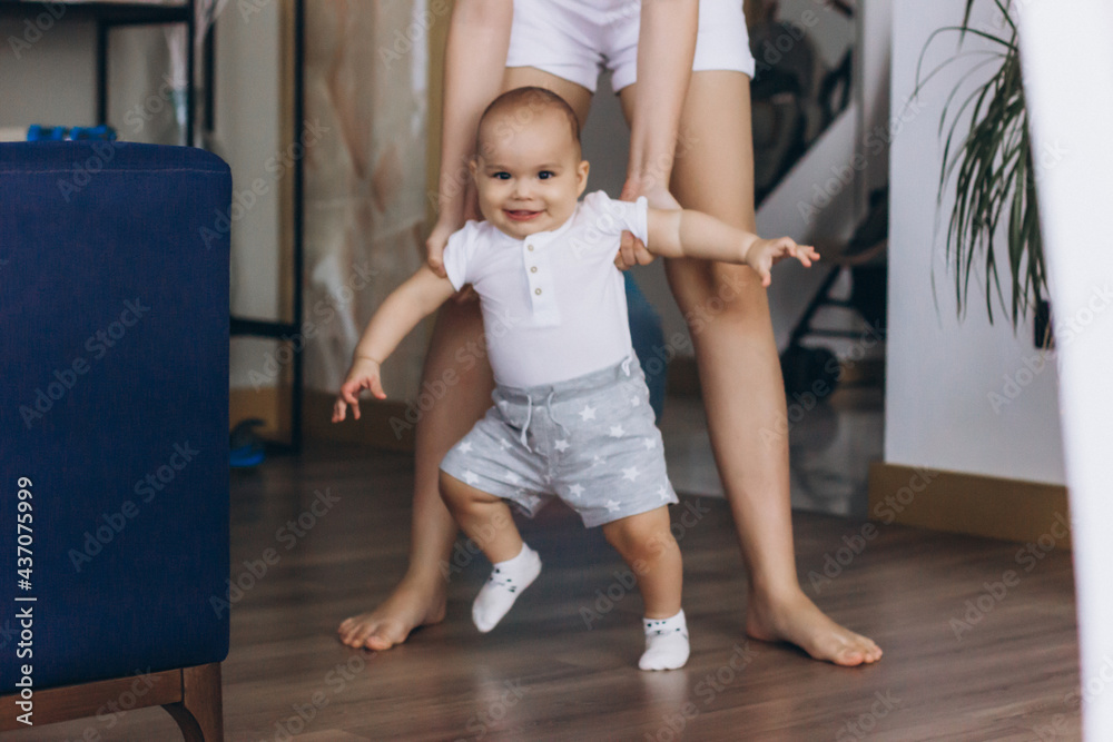 First steps of baby boy. Little child learning to walk. Mother helps ...