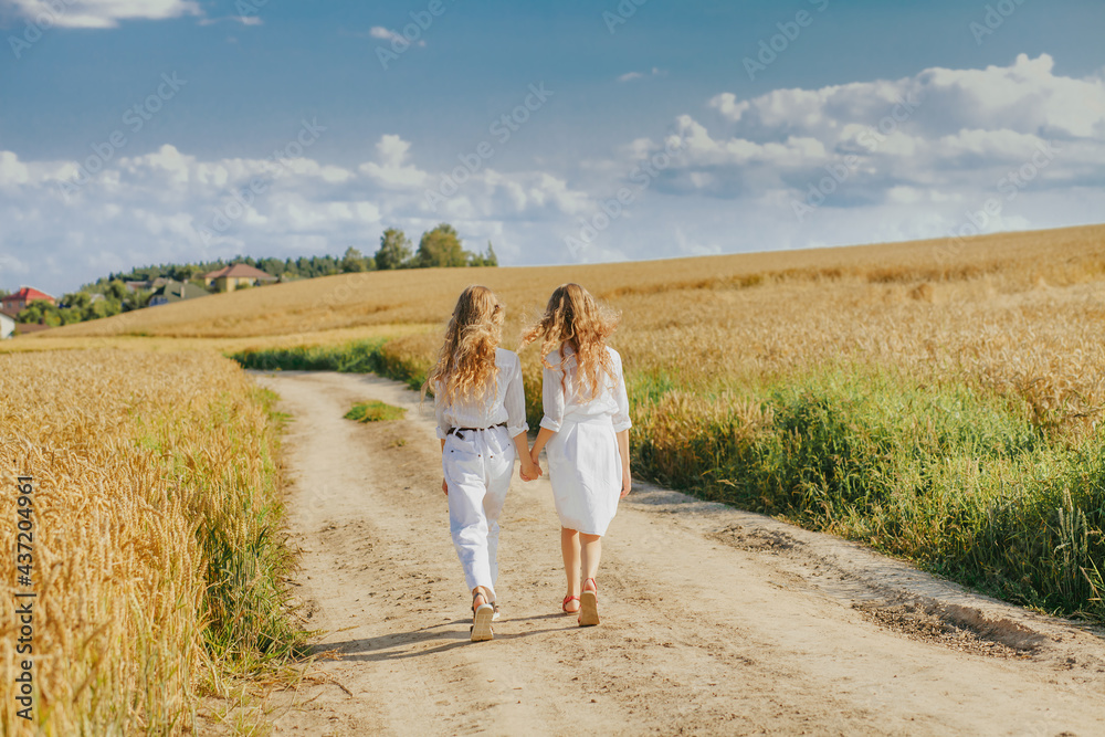 Two girls walk in countryside road. Outdoor photo of twins sisters ...