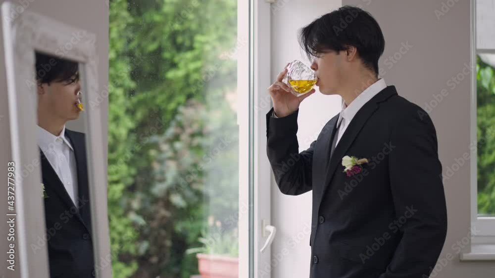 Vidéo Stock Confident wealthy Asian groom drinking whiskey looking out ...